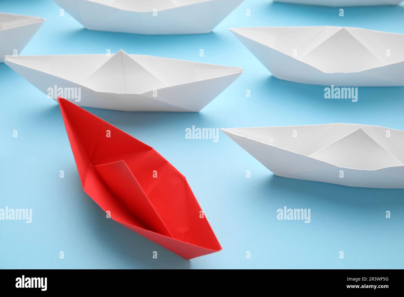 Red paper boat among others on light blue background, closeup ...