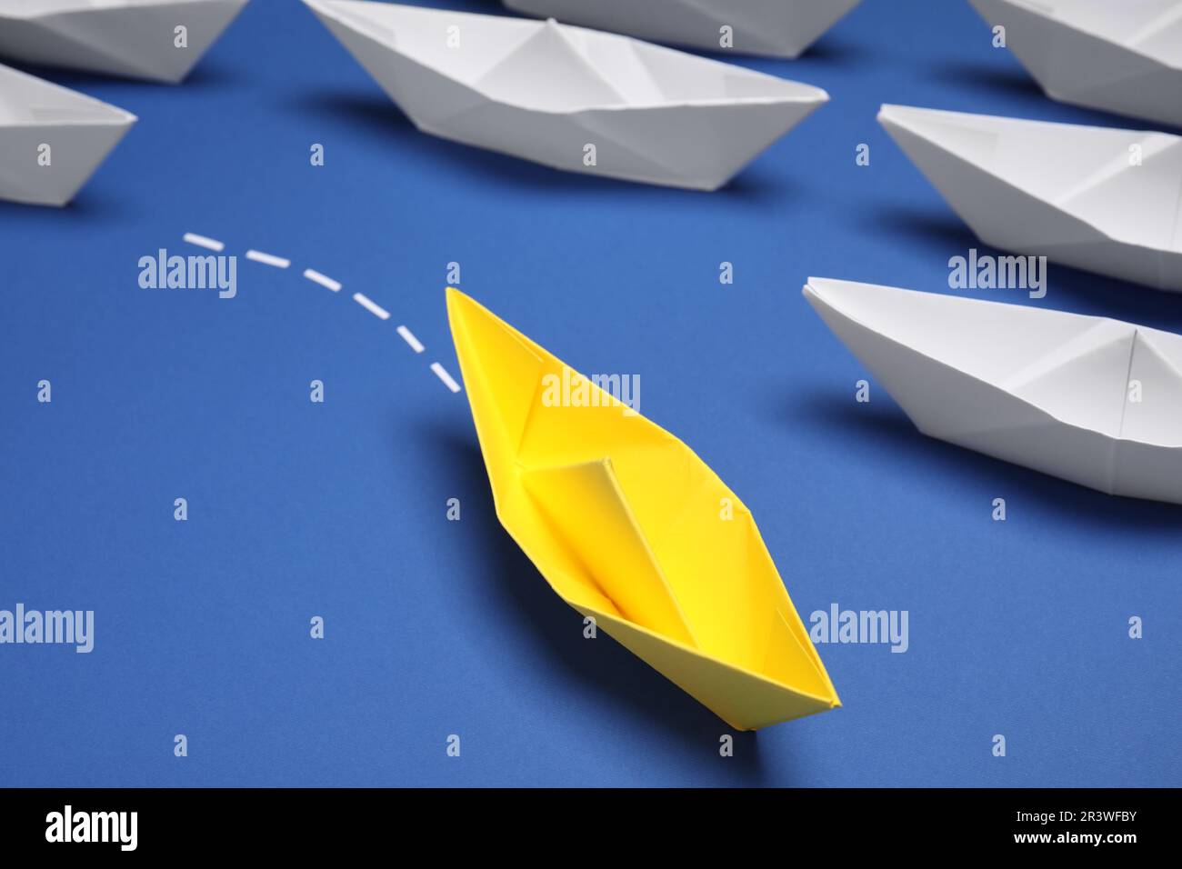 Yellow paper boat floating away from others on blue background, closeup ...