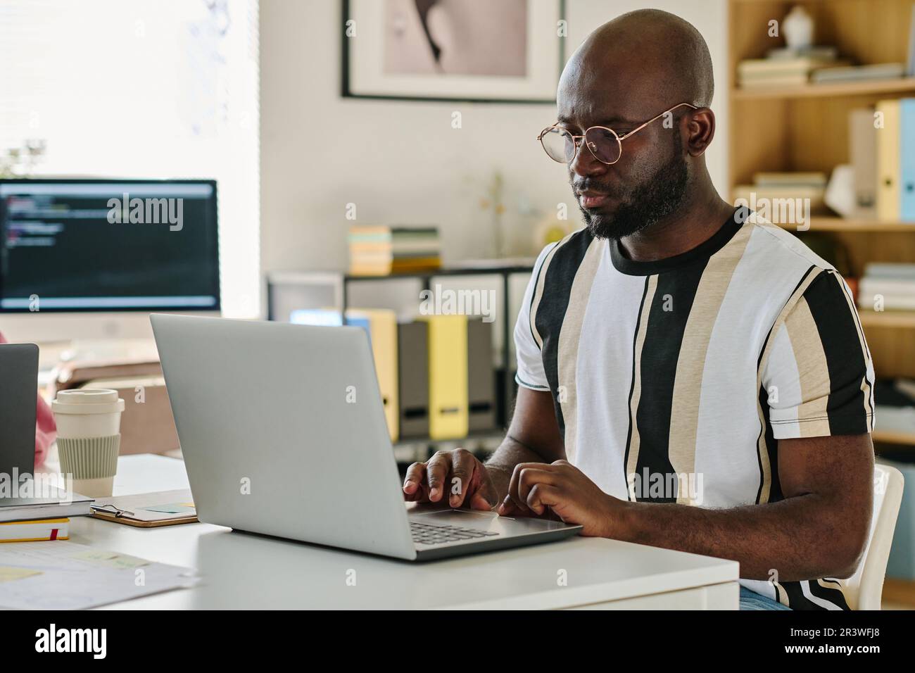 Serious African American programmer typing codes on laptop sitting at his workplace in IT office ...