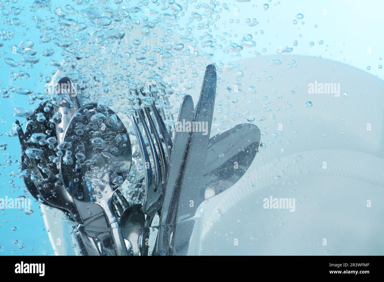 Washing silver cutlery and plates in water on light blue background ...