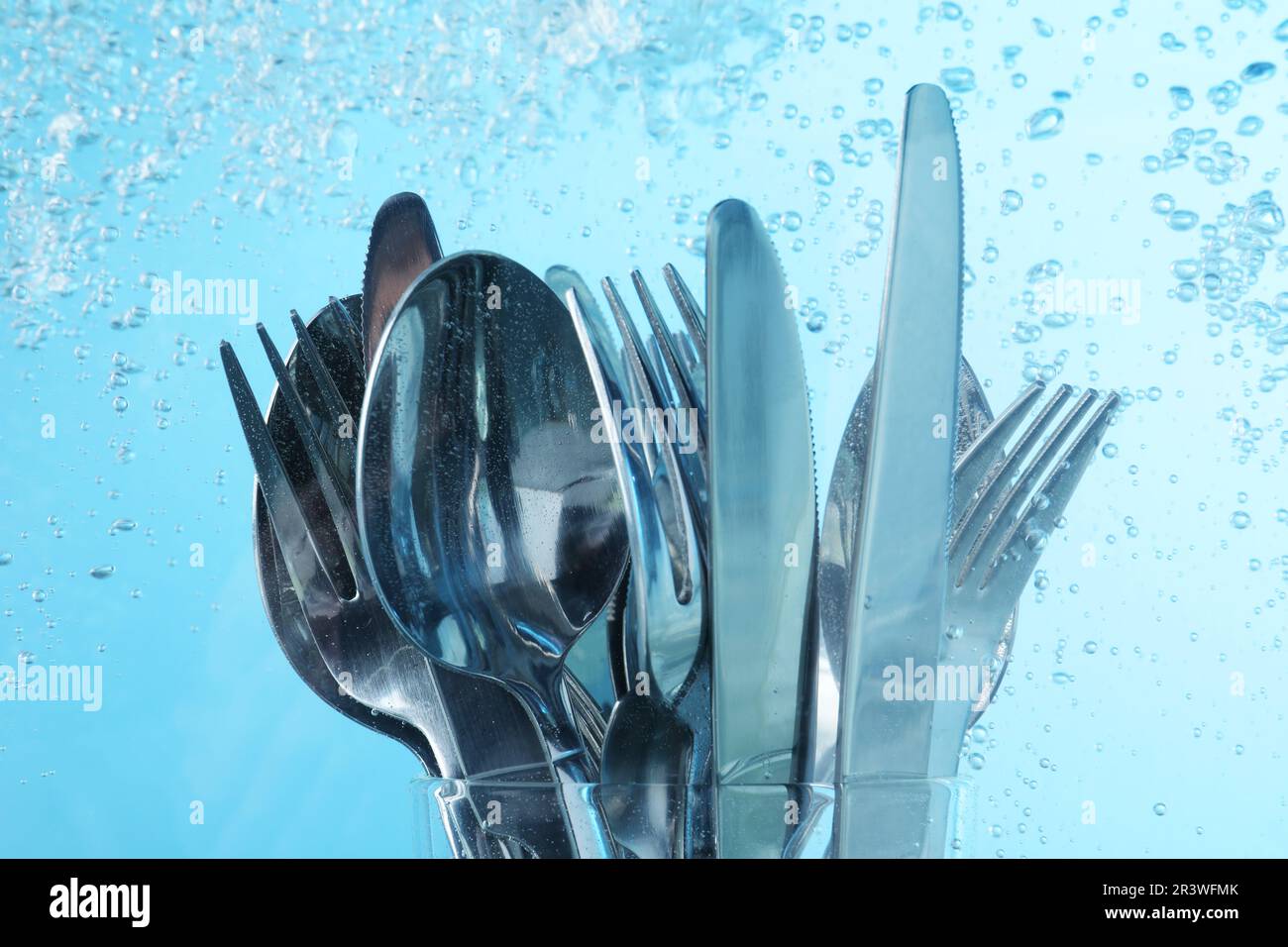 Washing silver cutlery in water on light blue background Stock Photo ...