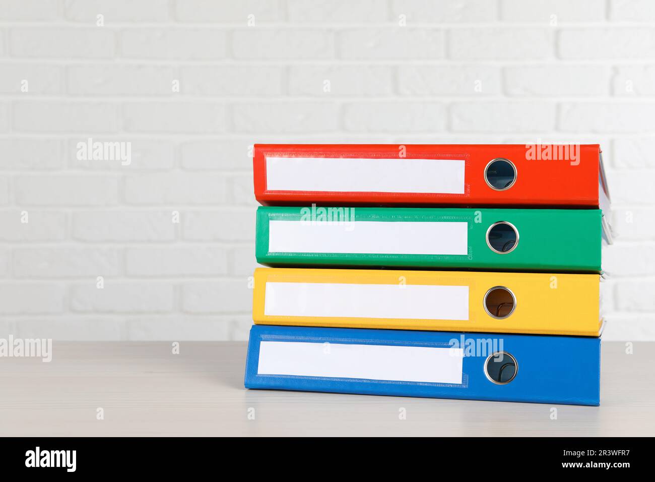 Stack of office folders on wooden table near white brick wall, space ...