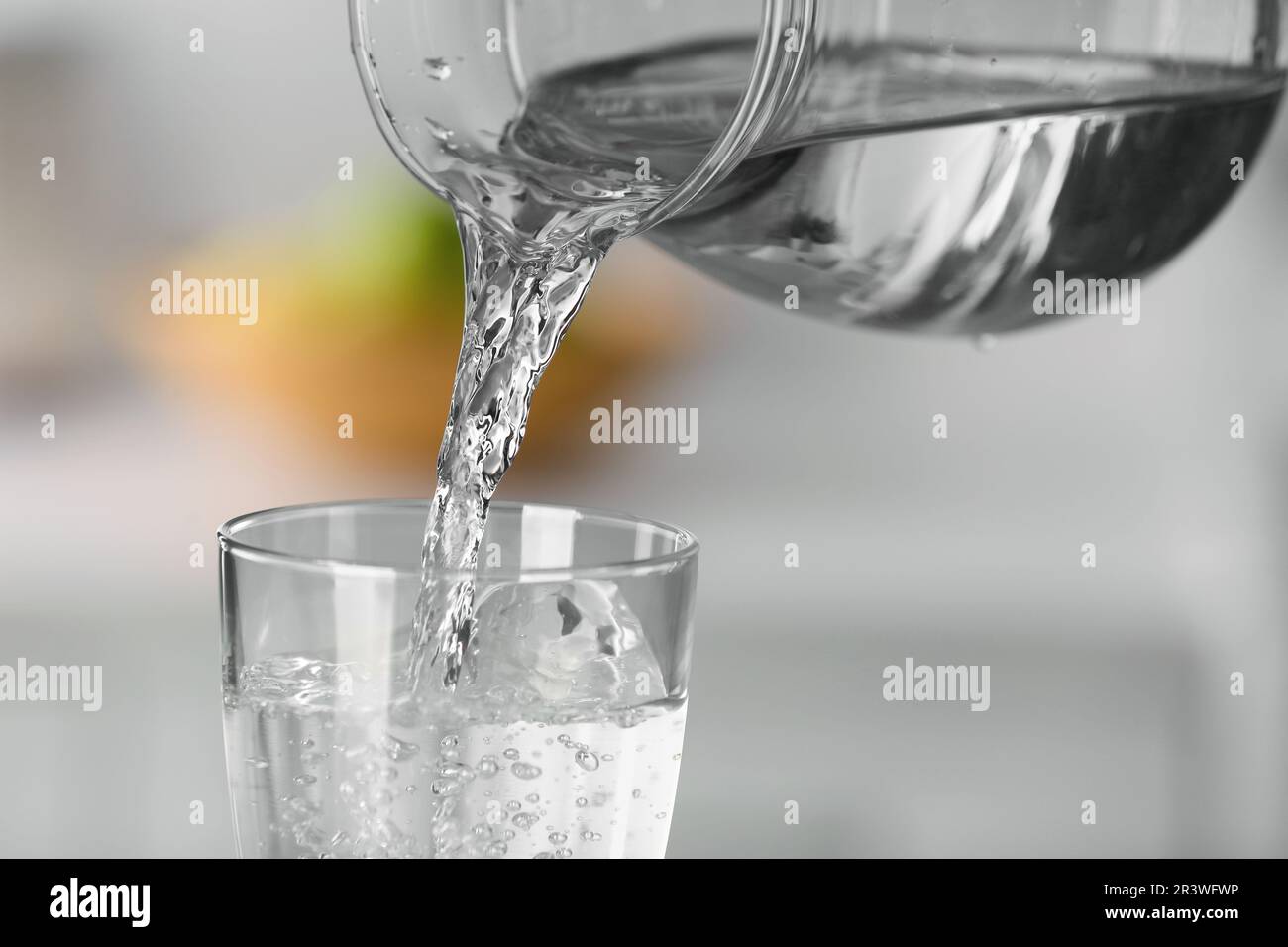 Pouring water from jug into glass on blurred background, closeup Stock ...