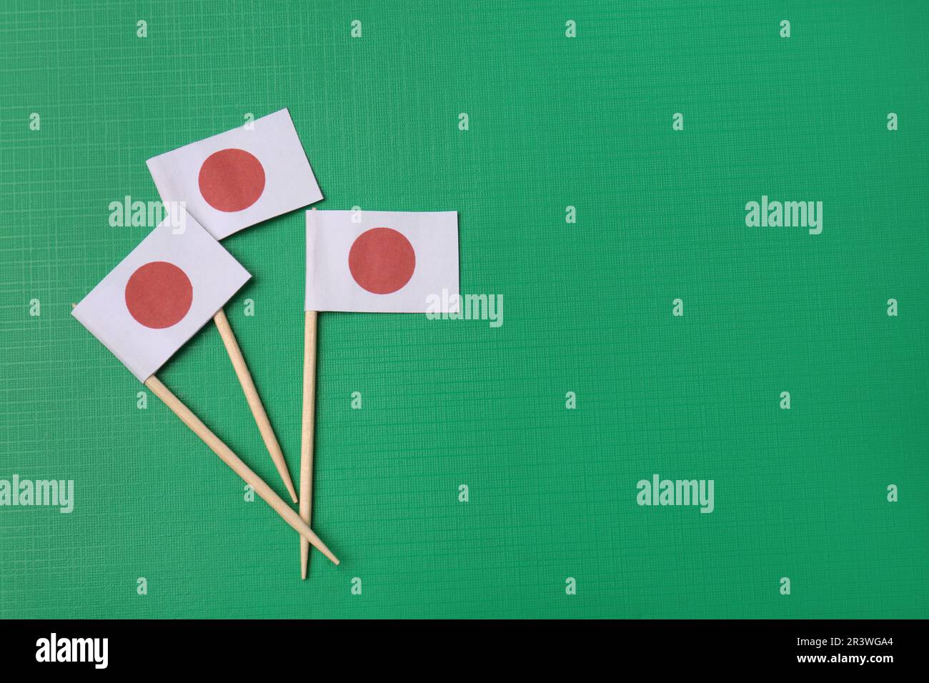 Small paper flags of Japan on green background, flat lay. Space for ...