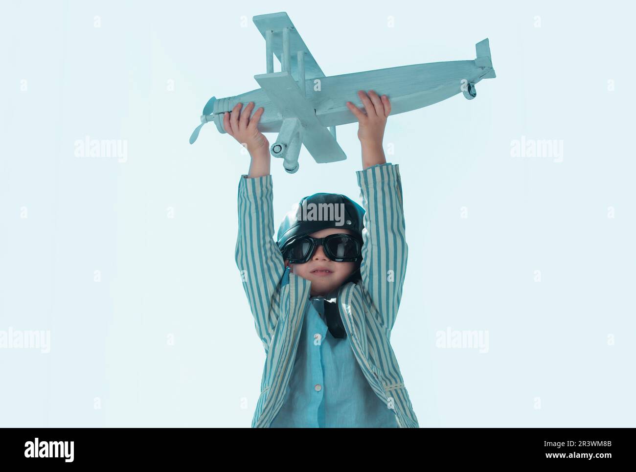 Kid with pilot goggles and helmet dreaming and plays with a toy plane ...