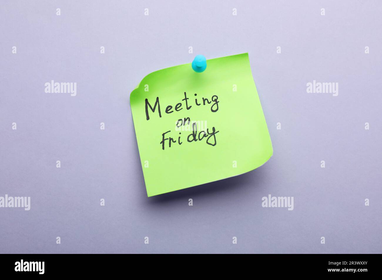 Paper note with words Meeting on Friday pinned to light grey background ...