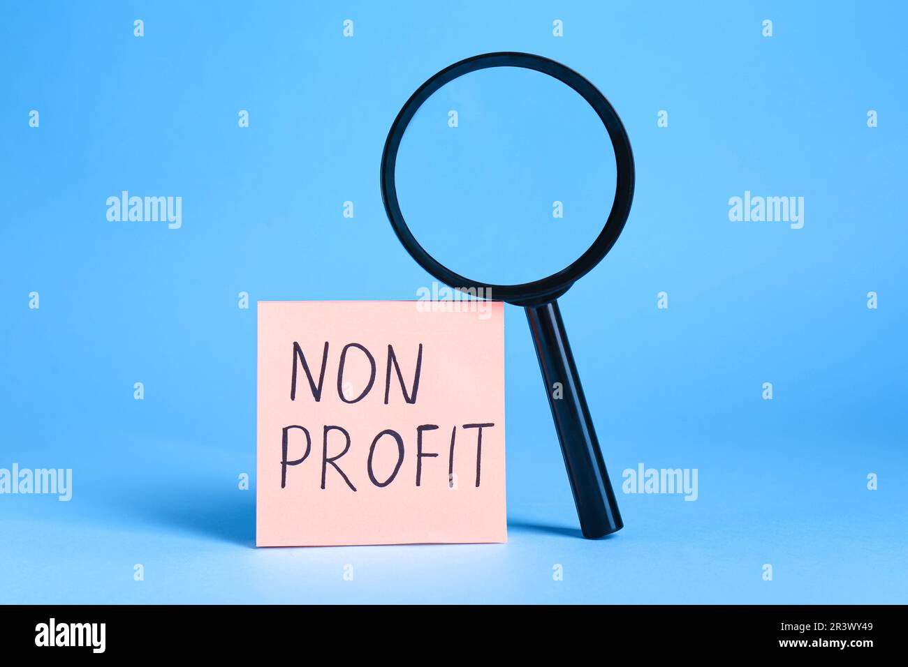 Paper note with phrase Non Profit and magnifying glass on light blue ...