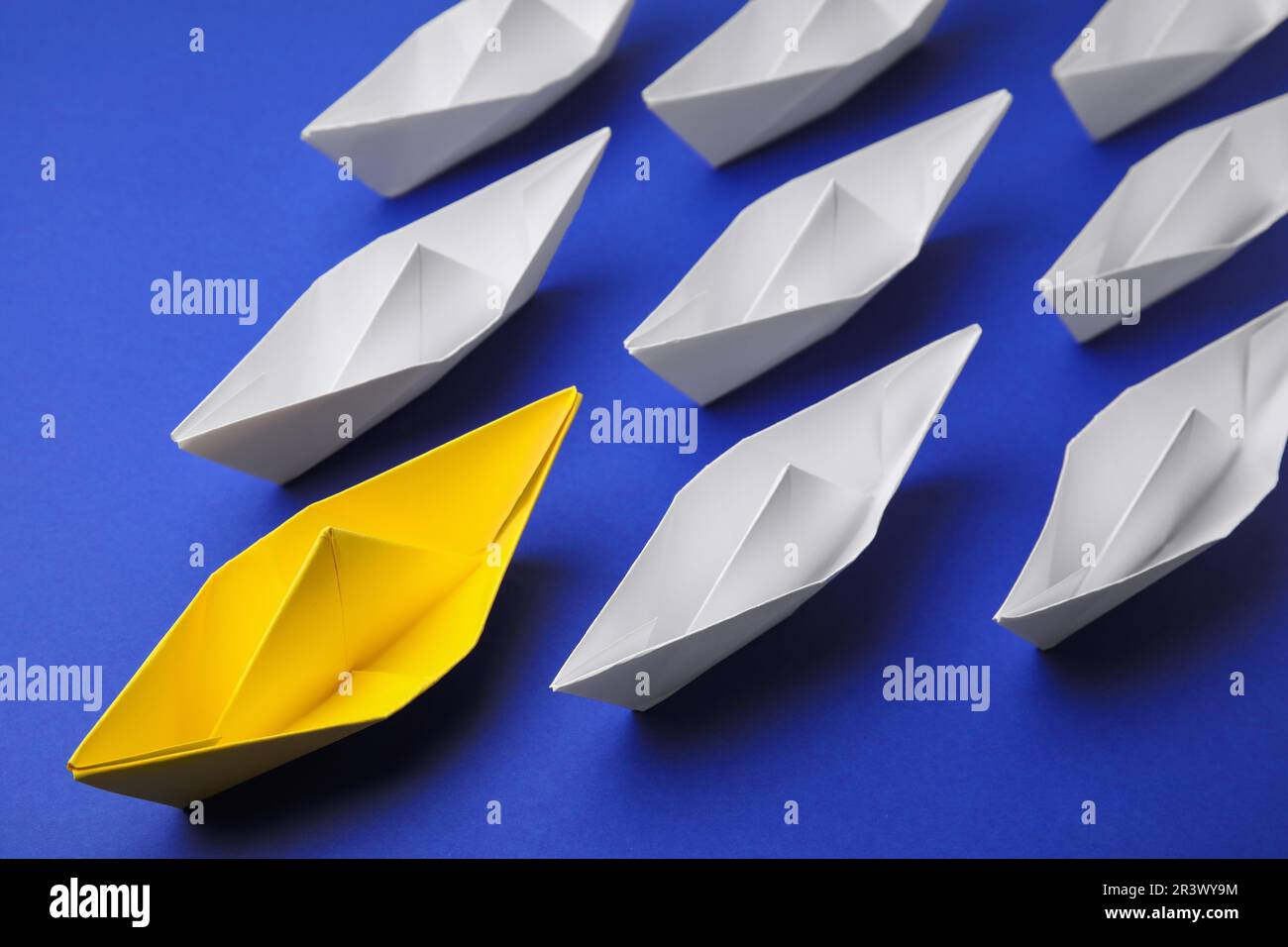 Yellow paper boat leading others on blue background, above view ...