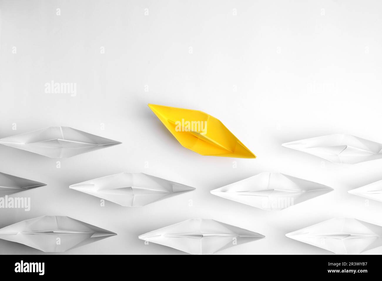 Yellow paper boat floating away from others on white background, flat ...