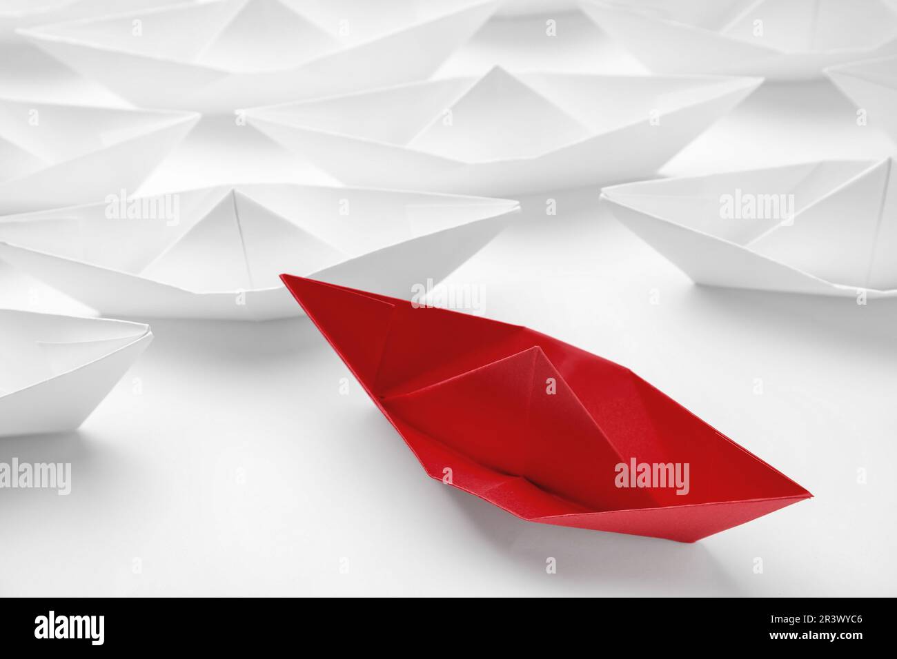 Red paper boat floating away from others on white background, closeup ...