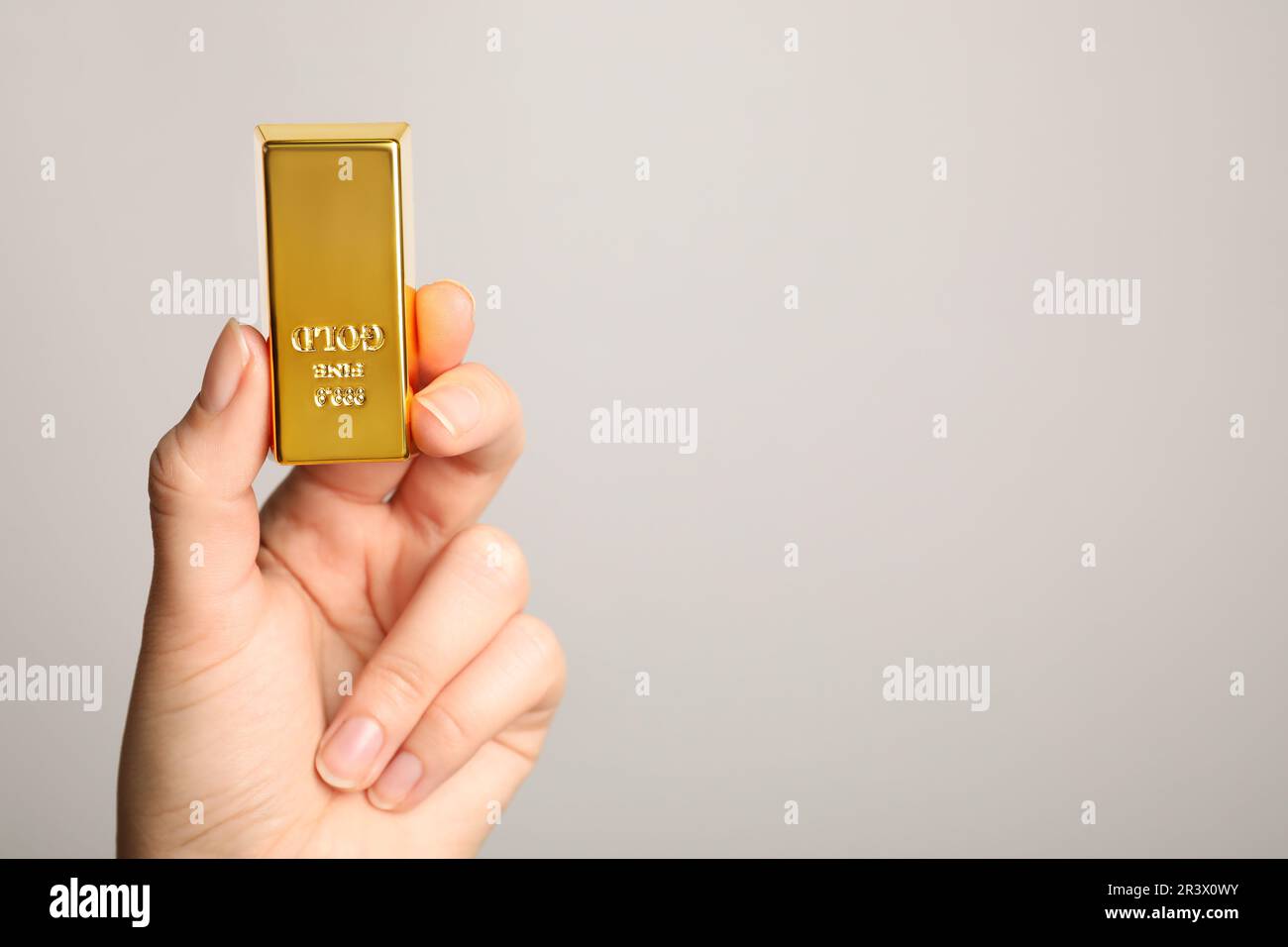 Woman holding shiny gold bar on light grey background, closeup. Space for text Stock Photo - Alamy