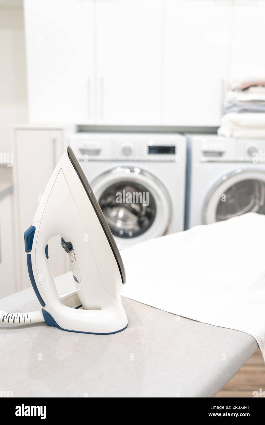 Iron on ironing board with white shirt in laundry room Stock Photo - Alamy