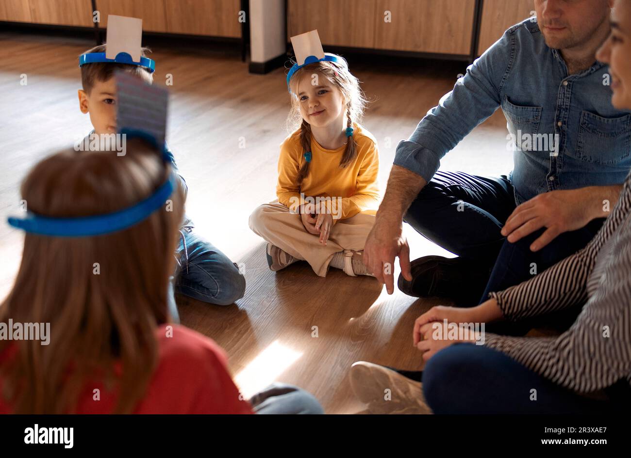 Happy young family with kids playing a card game at home sitting on the ...