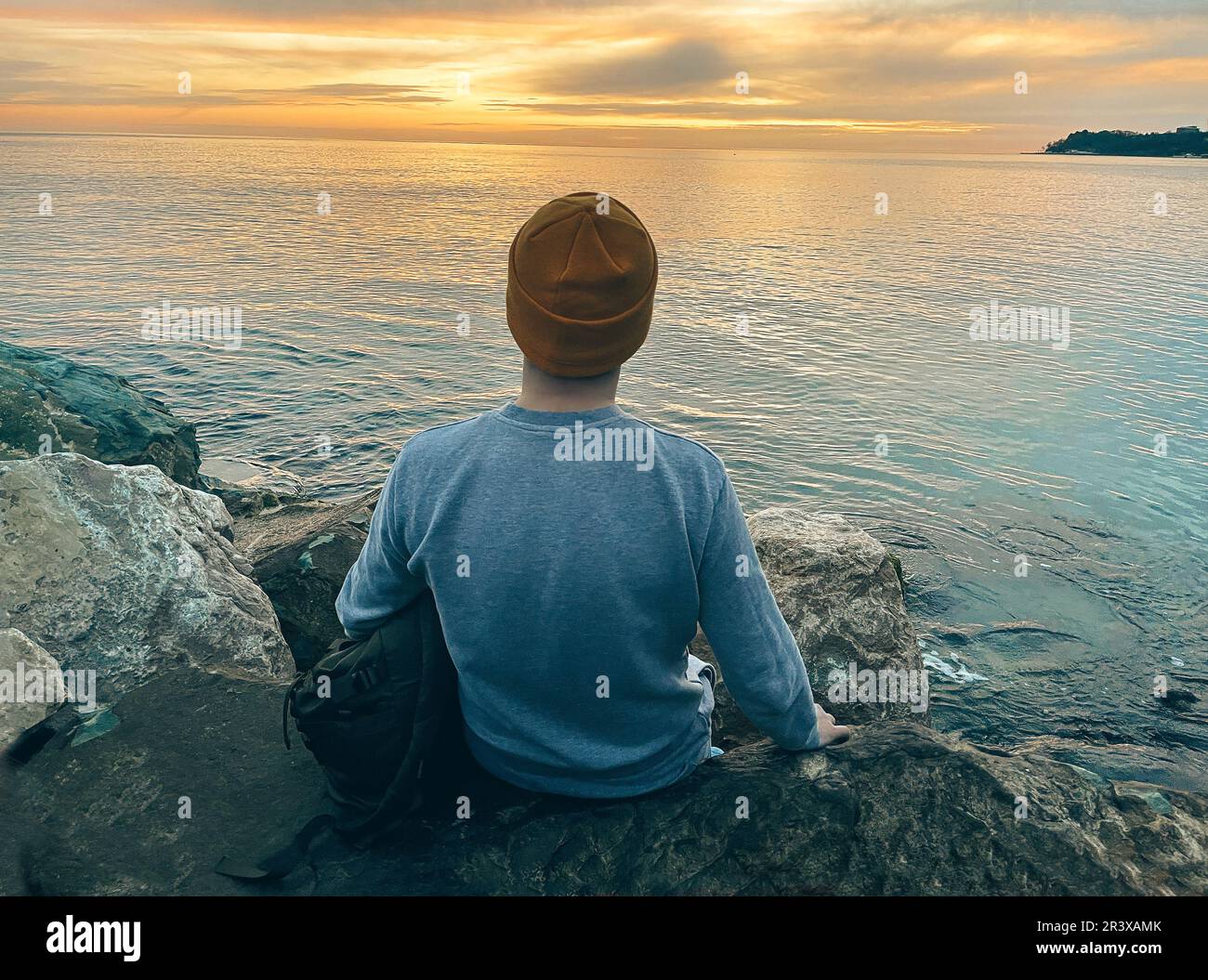 Young man in casual clothes sits on the rocks near the sea. Caucasian ...