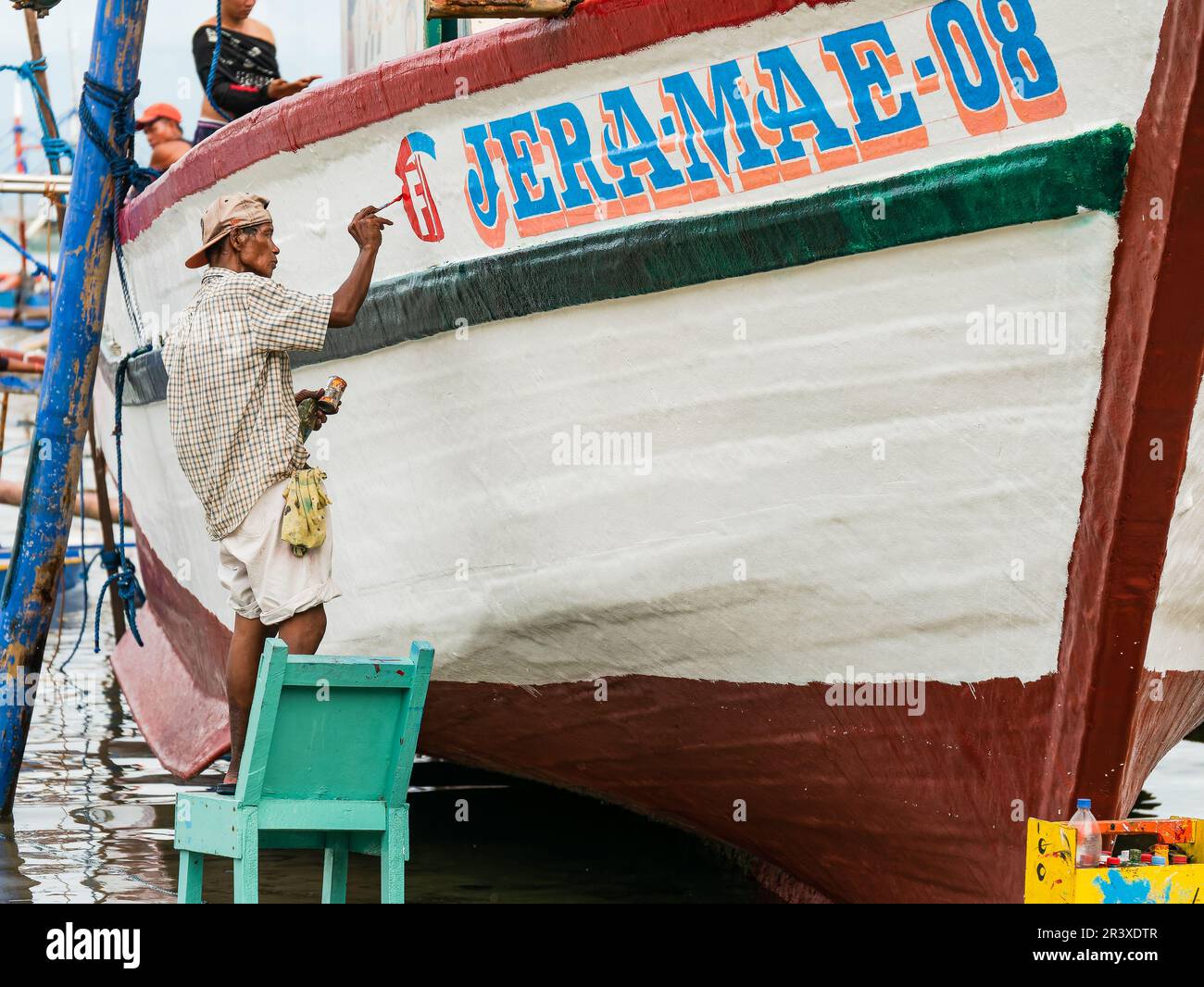 Man doing paint work on fishing vessel at basic shipyard on the beach ...