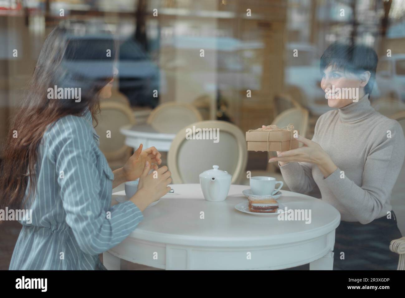 Young beautiful girl sitting in cafe with her friend and receiving a ...