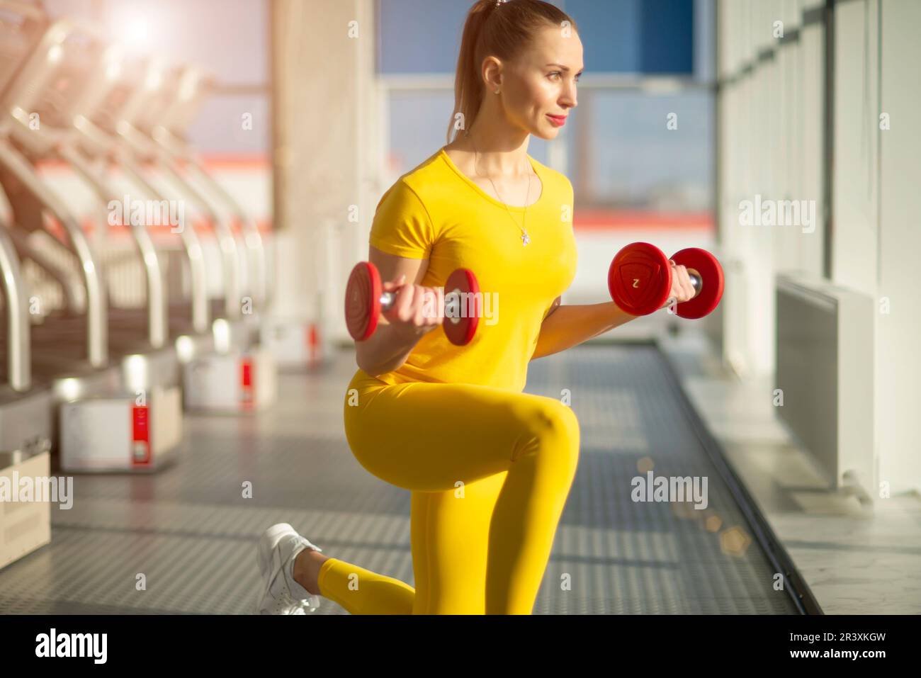 Physically fit pretty woman at the gym exercising with dumbbells to ...
