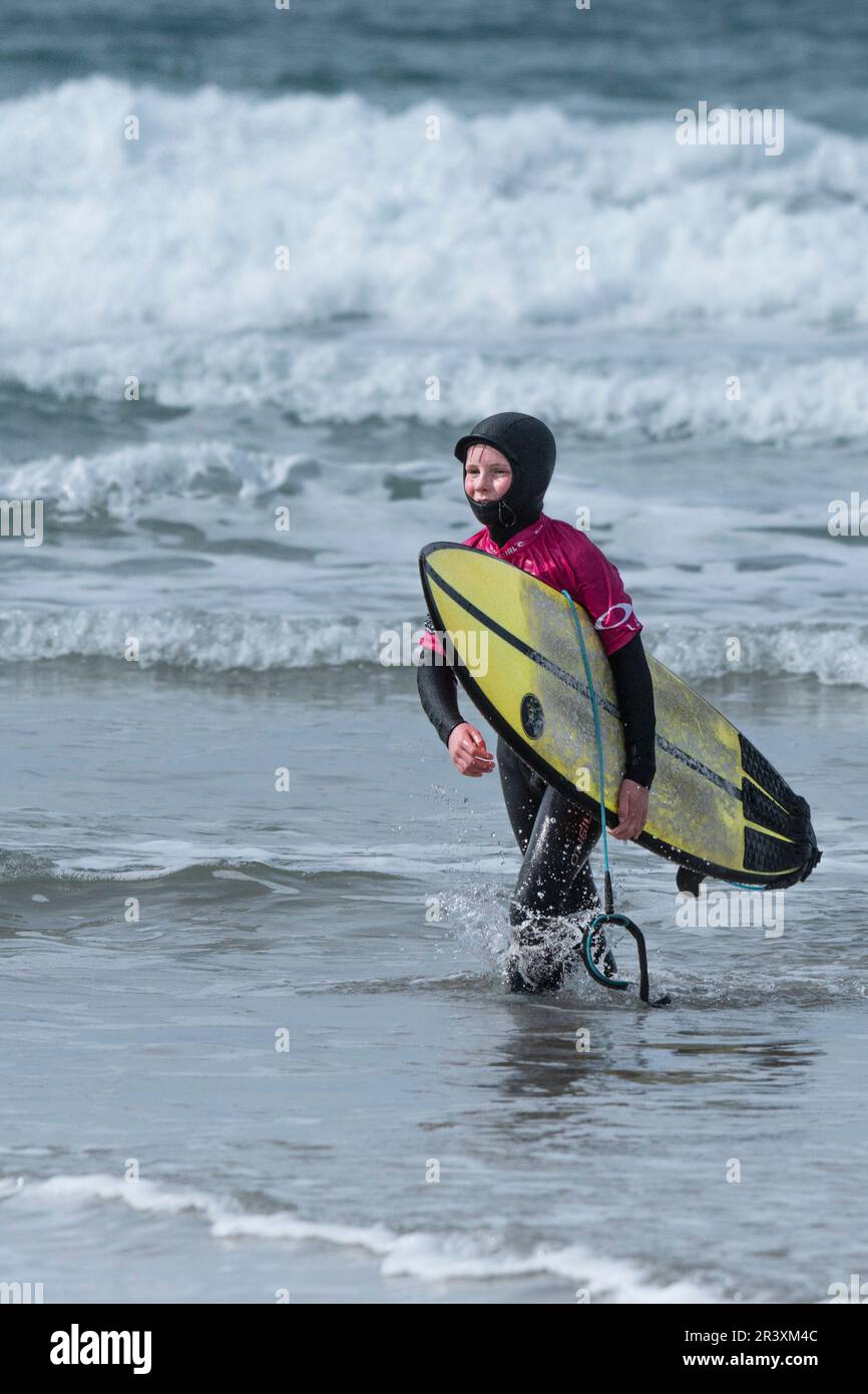 A young male surfer carrying his surfboard and walking out of the sea ...