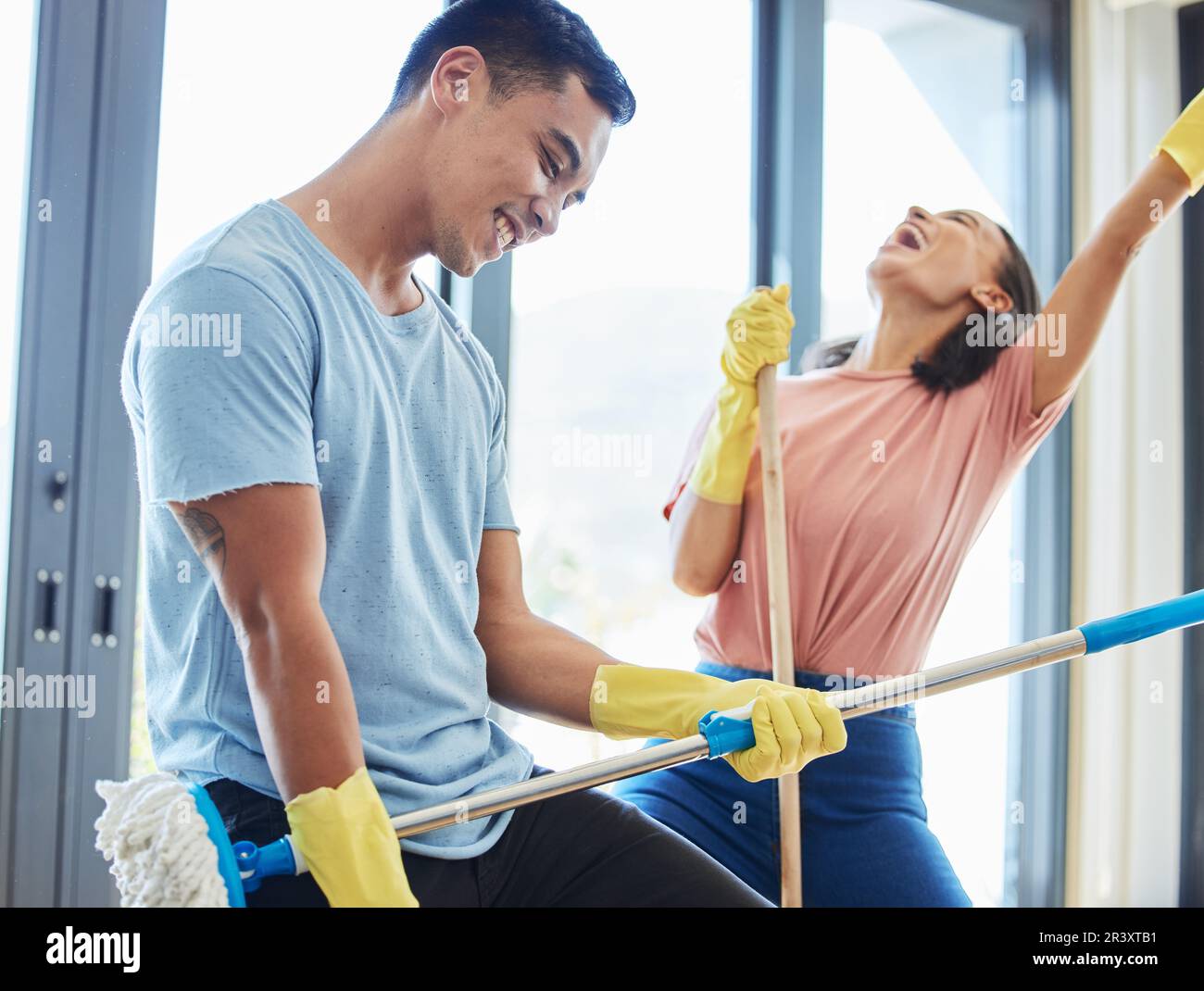 Couple, cleaning home and singing, dancing and having fun playing with mop guitar and broom ...