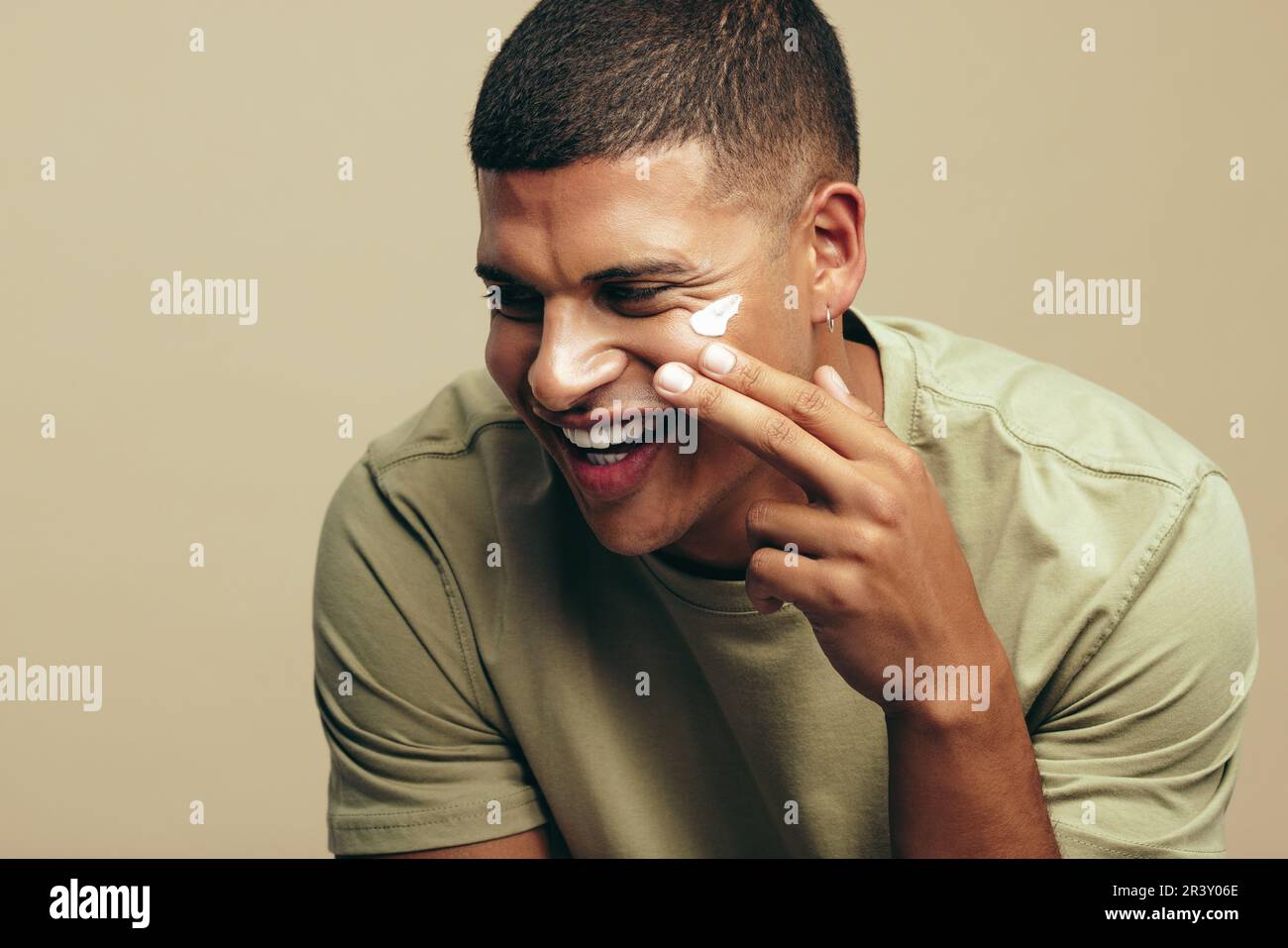 Young man smiling happily as he uses a moisturising facial cream on his skin in a studio ...