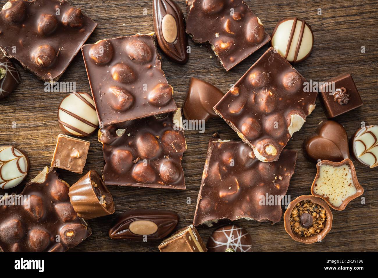 Broken chocolate bars with nuts and pralines on the wooden table. Top ...
