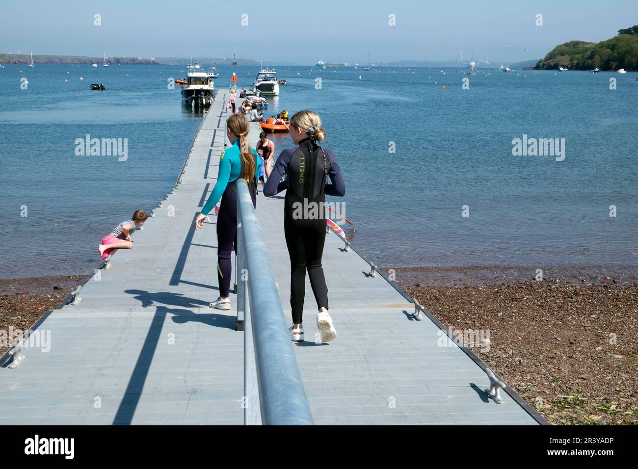 Rear back view of two girls wearing wetsuits walking along pontoon with ...