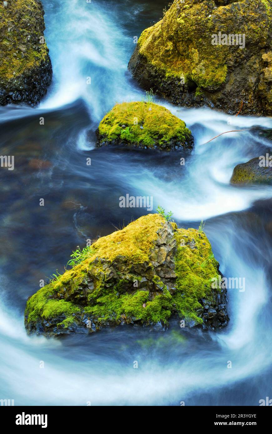 blue water rushing around green river rocks Stock Photo - Alamy
