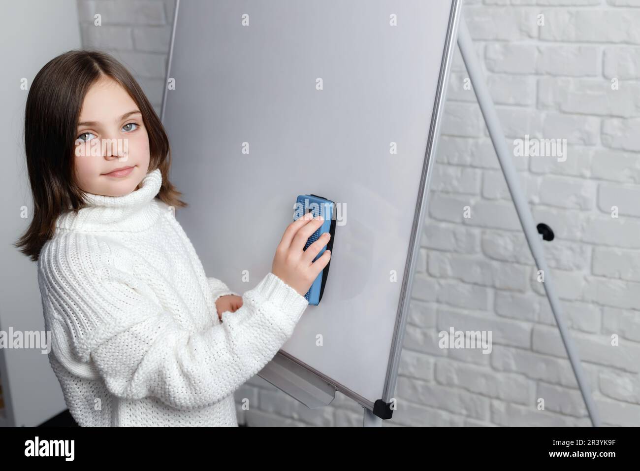 Little girl standing and cleaning whiteboard. Child smiling and looking ...