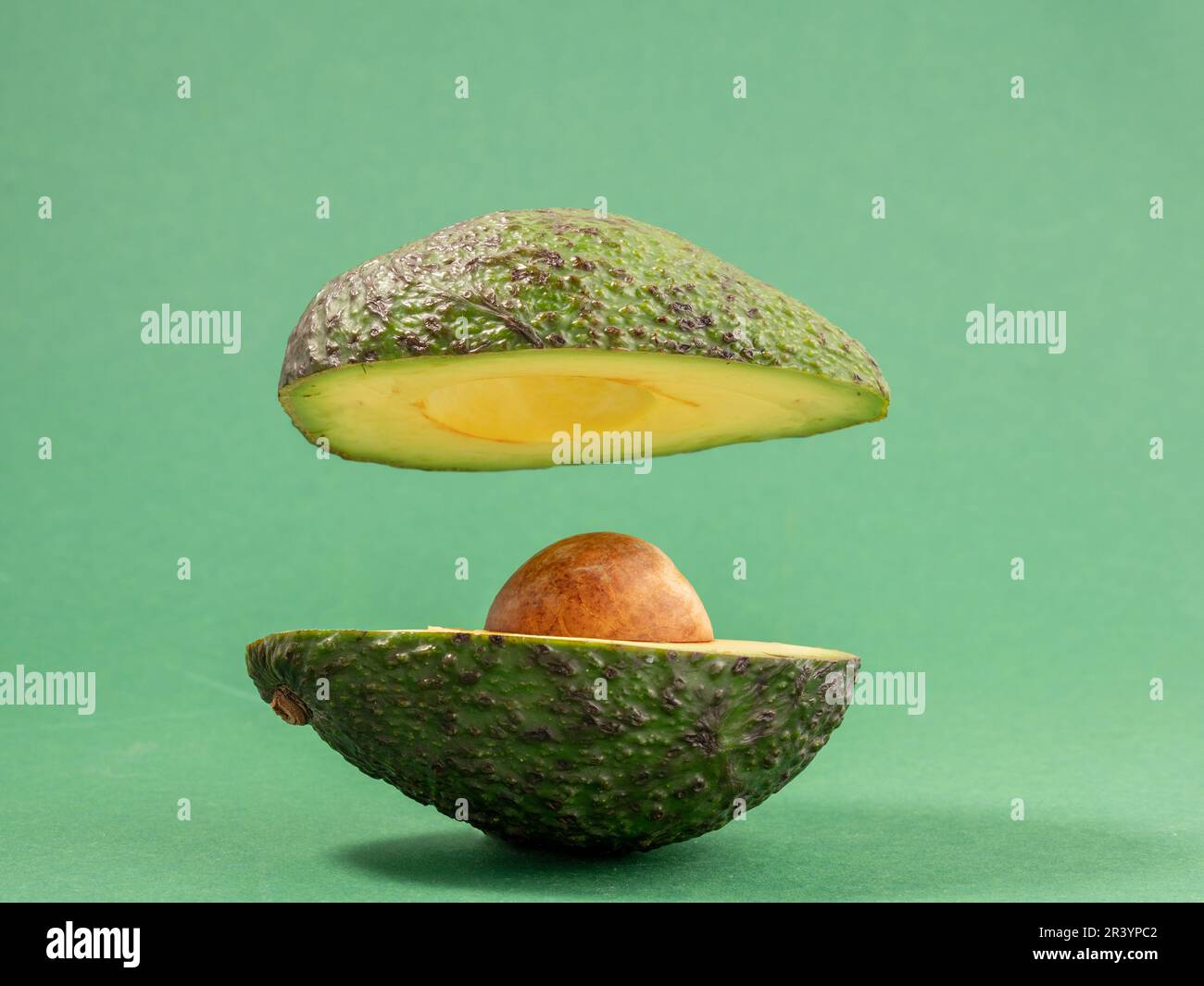 Two halves of a green avocado and the core of the fruit float in the ...