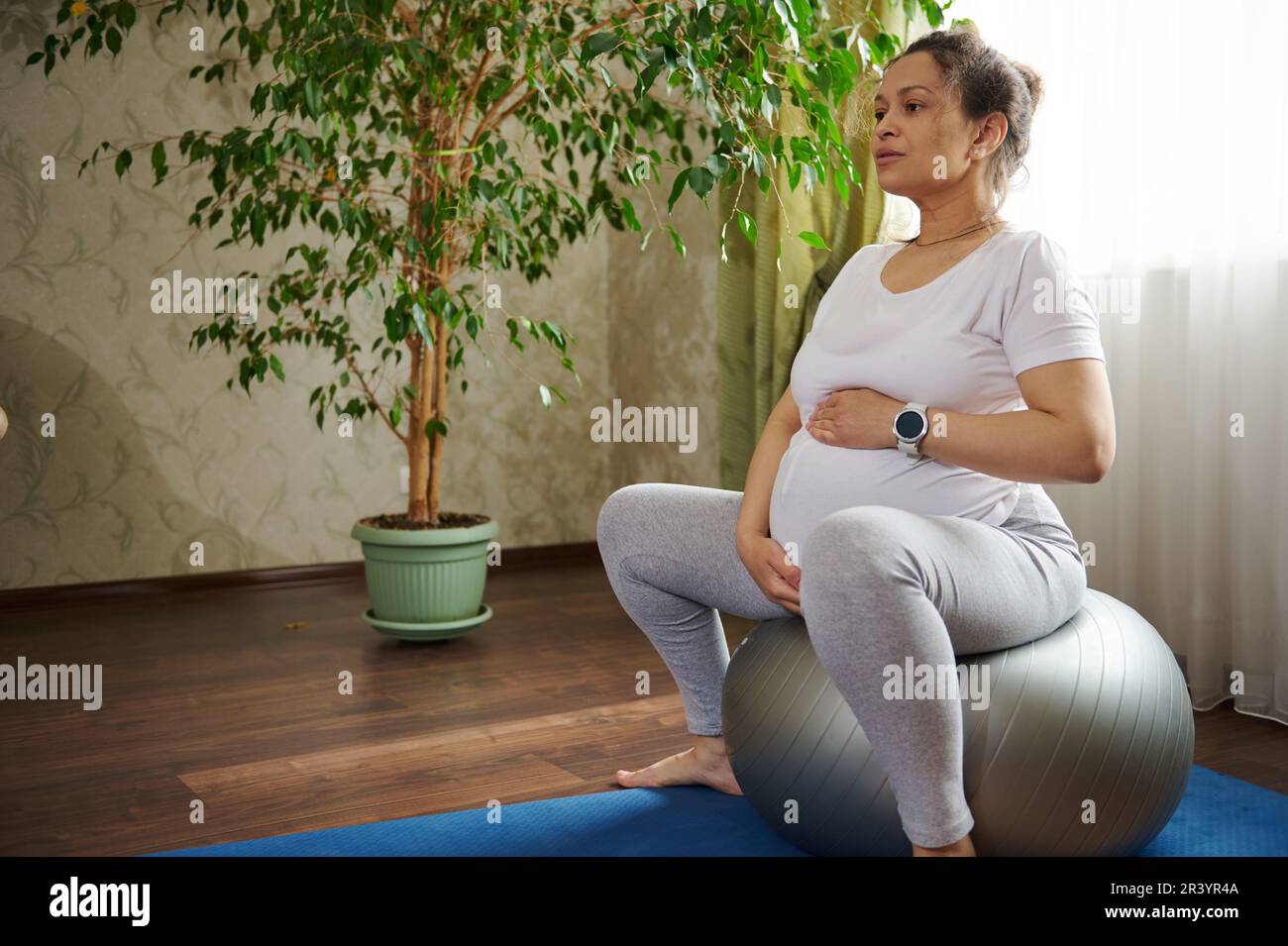 Active pregnant woman holds hands on belly, performs prenatal breathing ...
