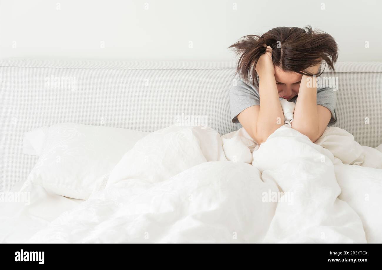 Upset sad young brunette woman sitting in bed at home, with copy space ...