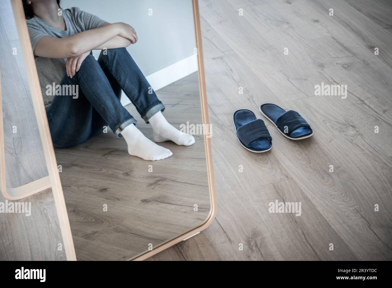 Reflection in mirrow of a sad woman sitting on a floor alone in empty ...