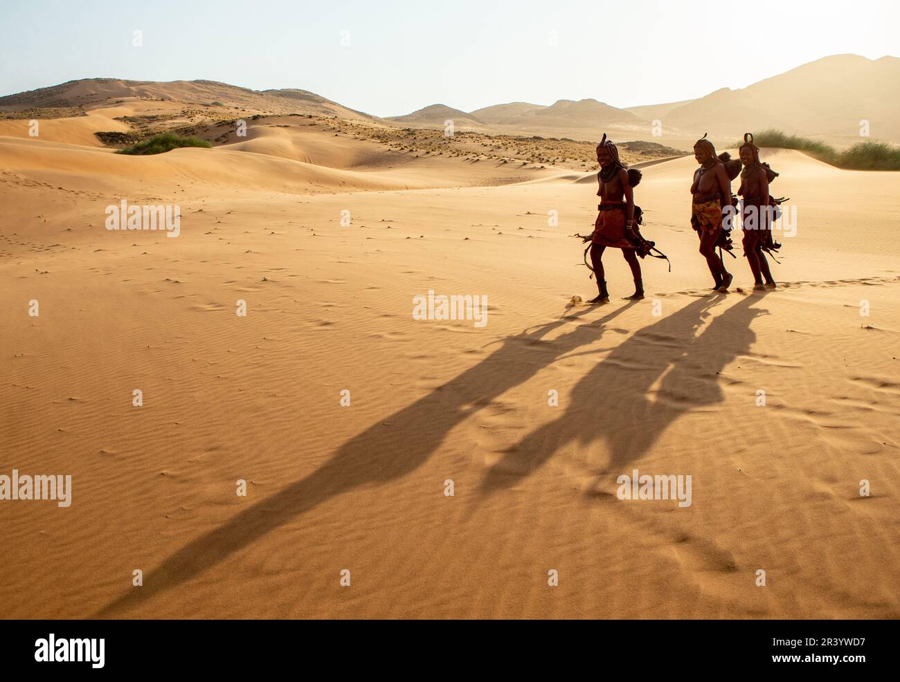 Three women of the Himba tribe in traditional dress walk in the desert ...