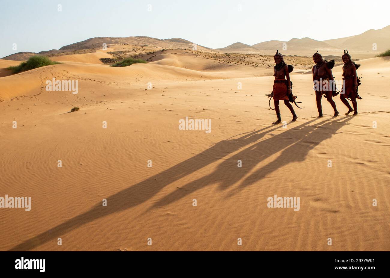 Three women of the Himba tribe in traditional dress walk in the desert ...