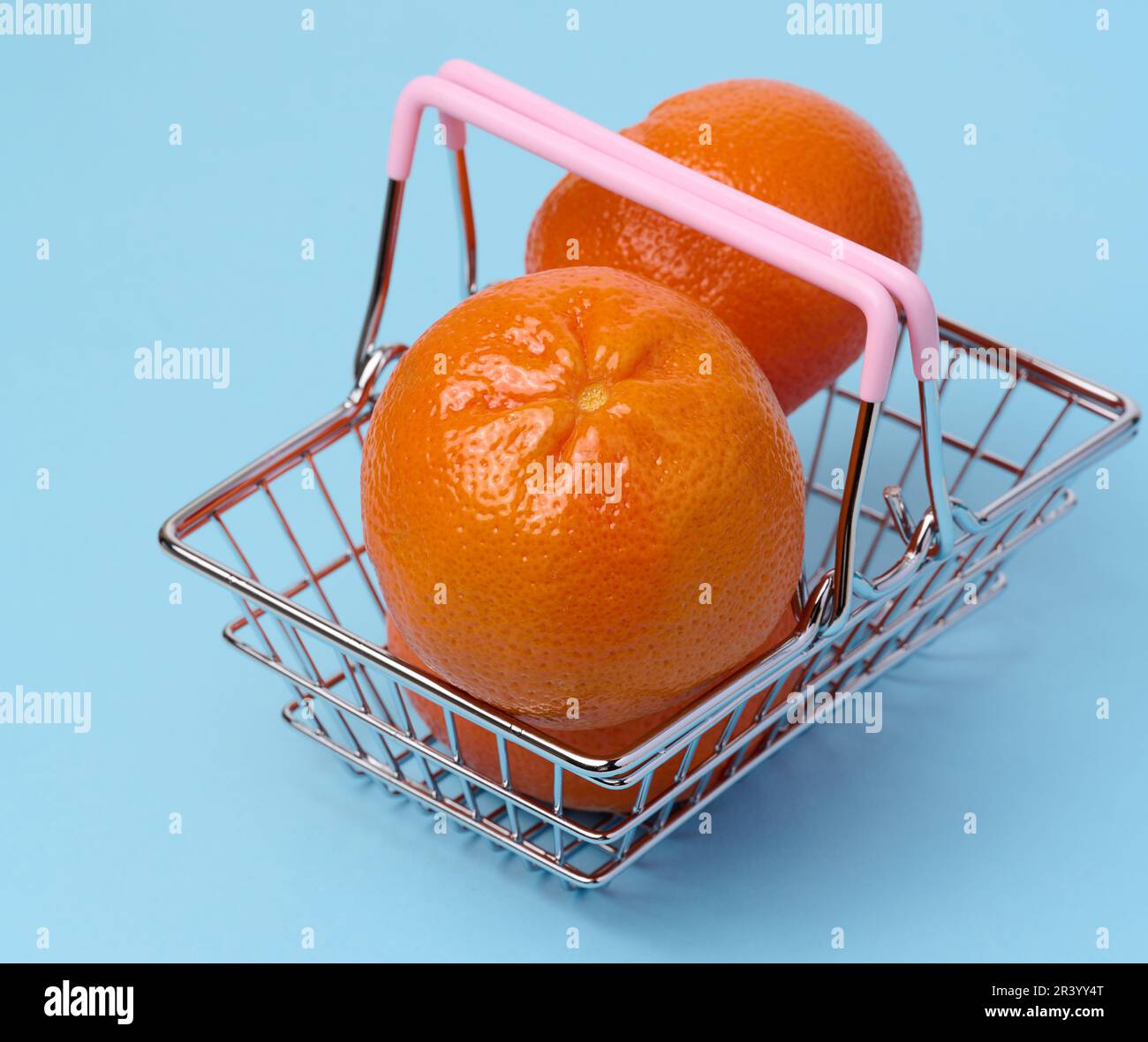 Ripe mandarins in a miniature metal shopping cart on a blue background ...