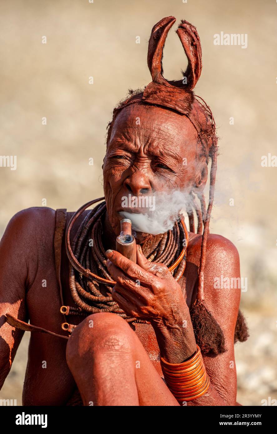 Portrait of an old woman of the Himba tribe with a smoking pipe in her ...