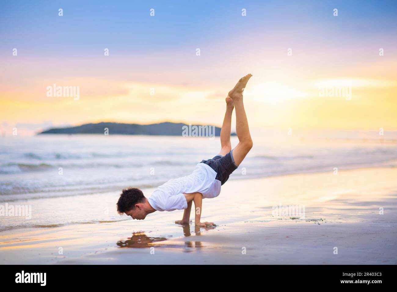 Teenager doing calisthenics exercise. Beach yoga at sunset. Teen boy ...