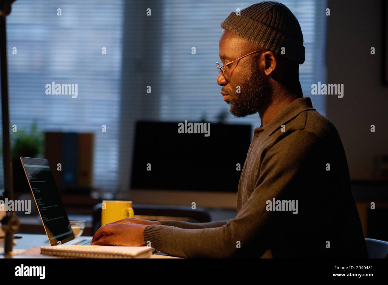Side view of African American programmer concentrating on his online work with codes on laptop ...