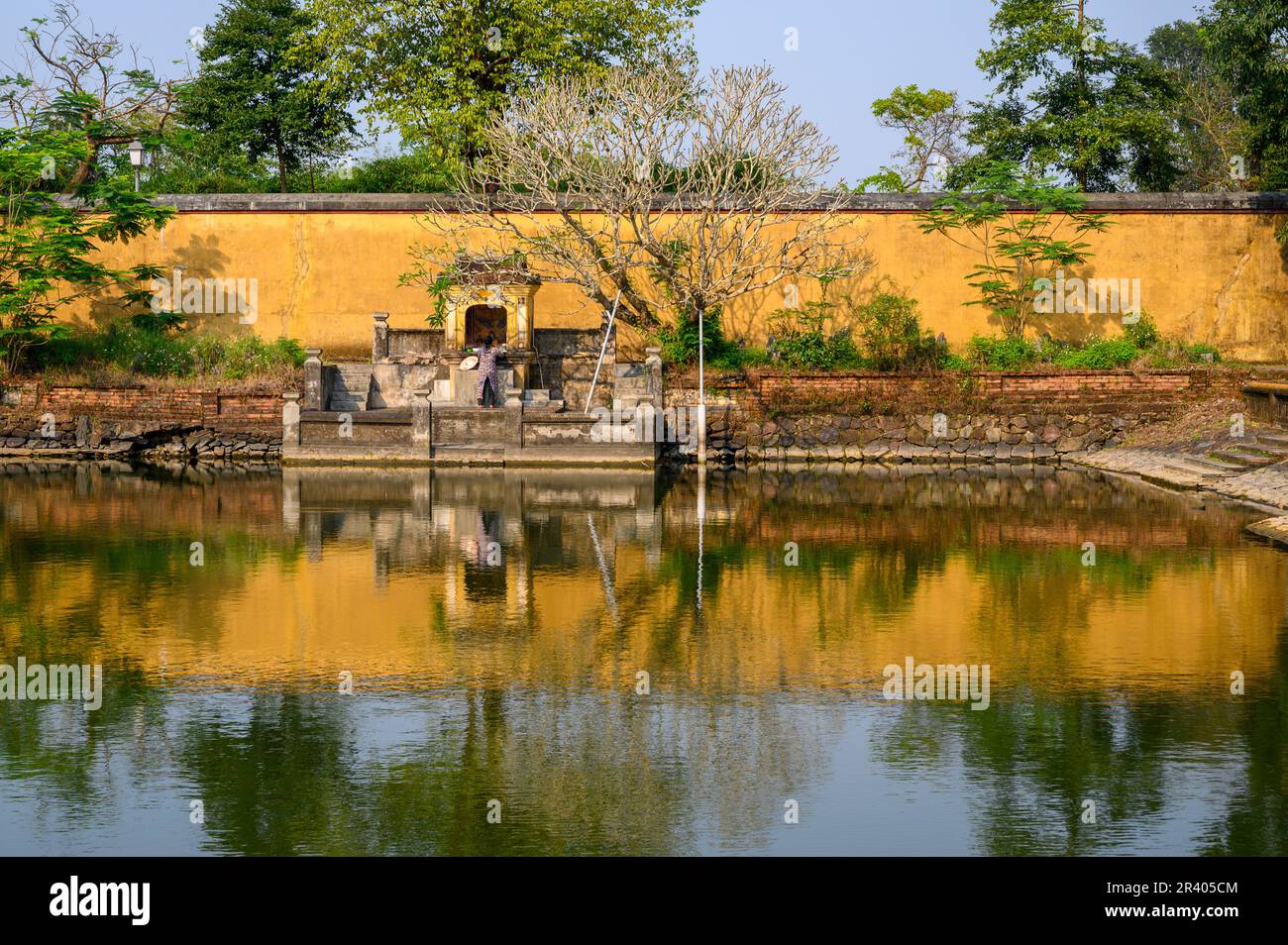 A yellow wall, trees and a shrine reflecting on a pond in the Imperial ...