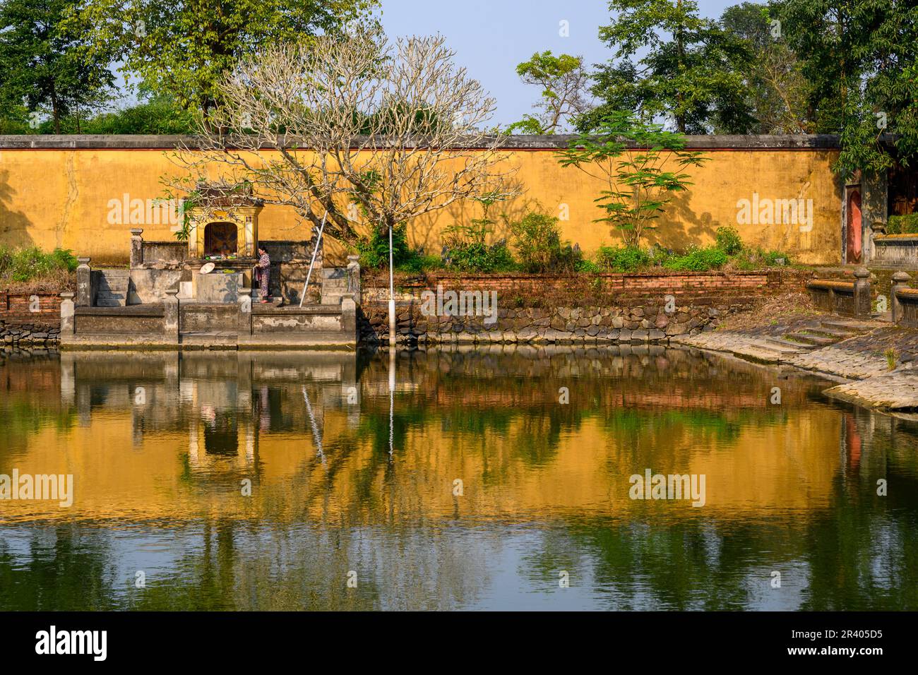 A yellow wall, trees and a shrine reflecting on a pond in the Imperial ...