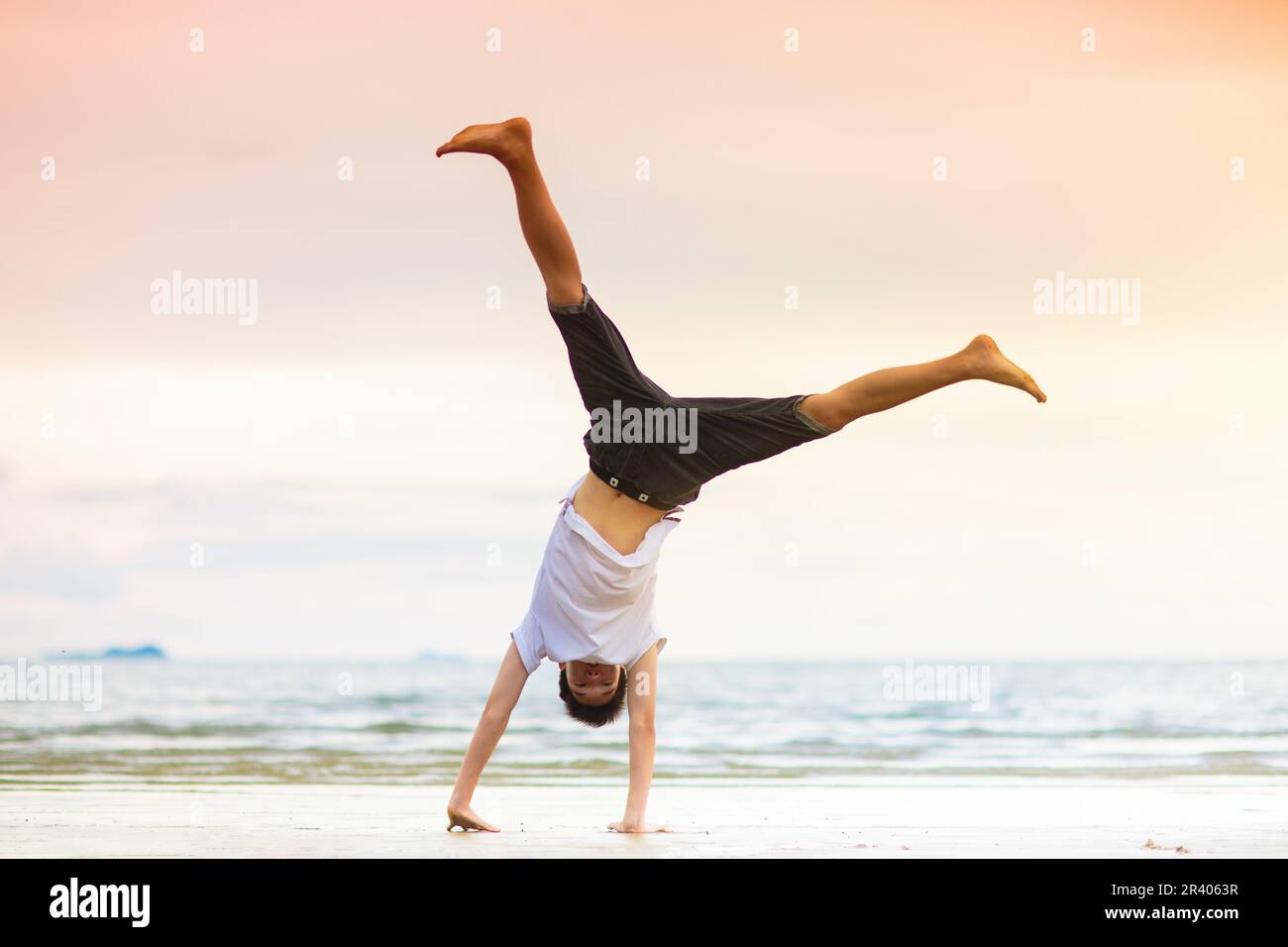 Teenager doing calisthenics exercise. Beach yoga at sunset. Teen boy ...