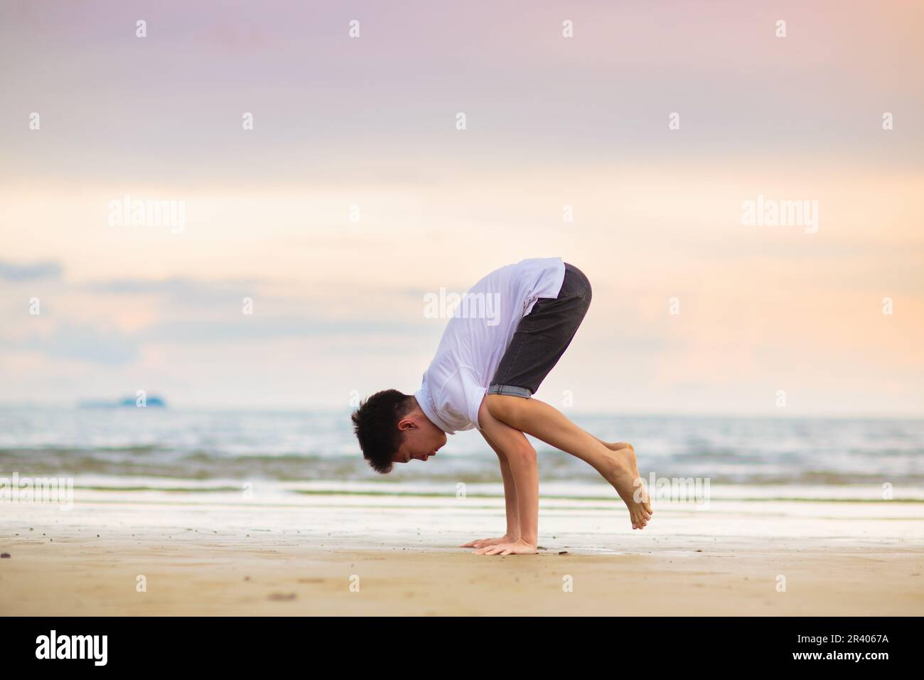 Teenager doing calisthenics exercise. Beach yoga at sunset. Teen boy ...