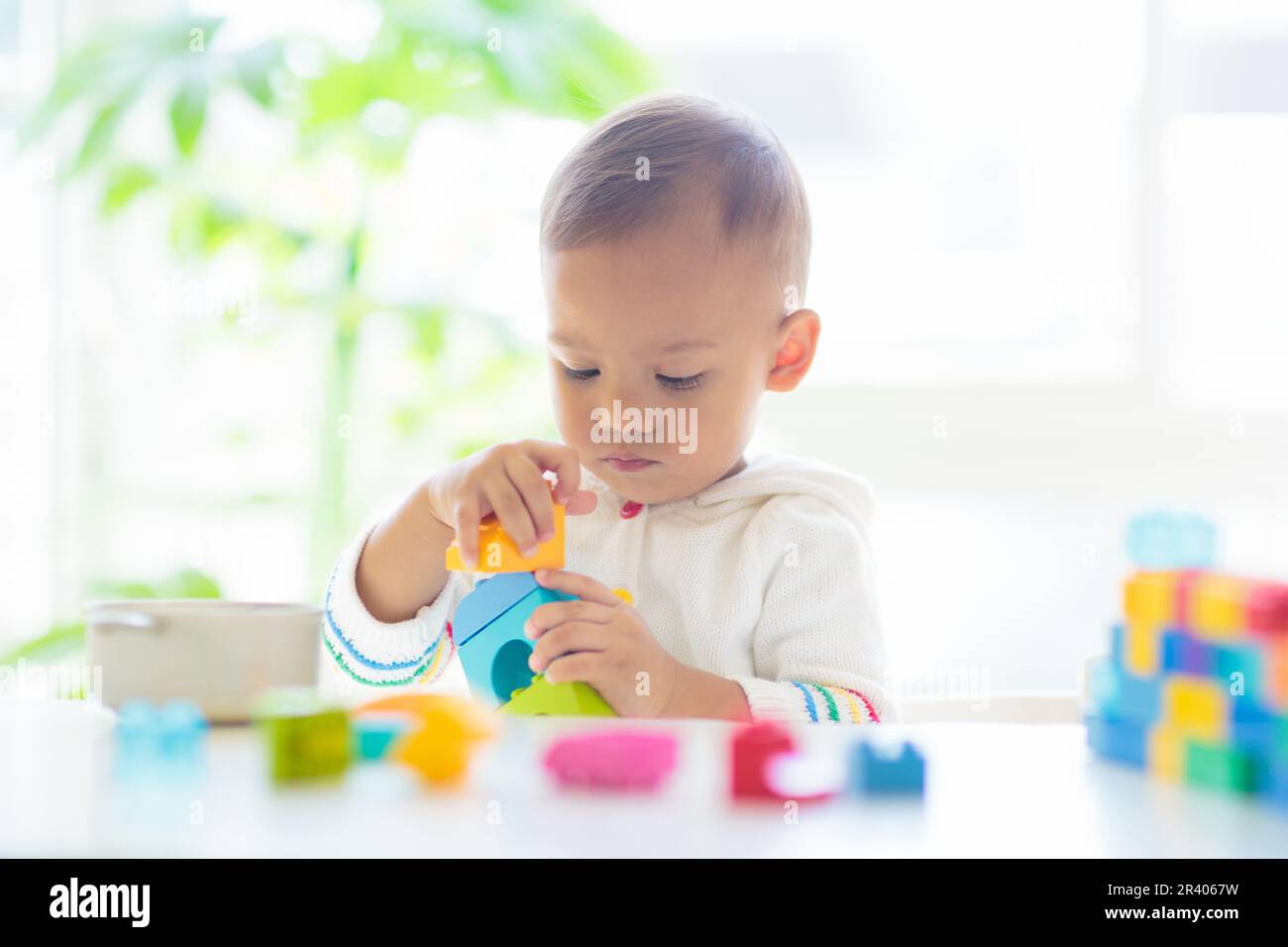 Adorable Asian baby boy playing with colorful blocks toy in white sunny ...