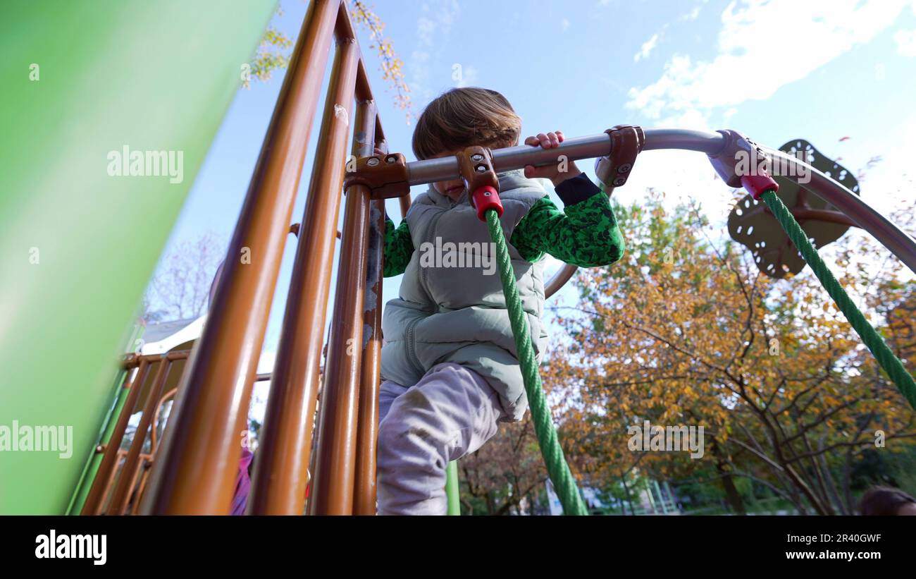 Little boy exercising outside holding in metal bar at playground ...