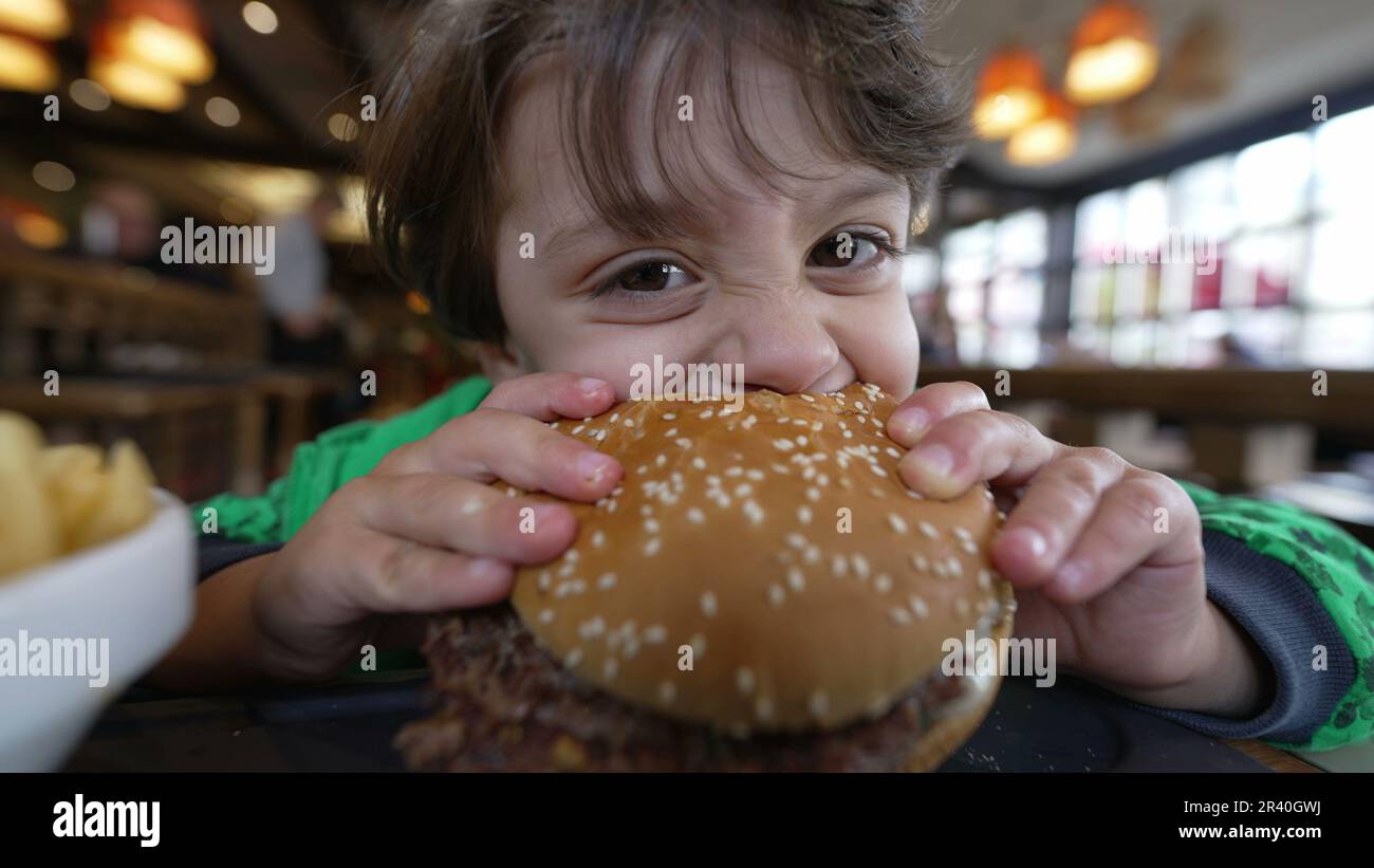 Hungry small boy eating burger sitting inside restaurant place. One ...