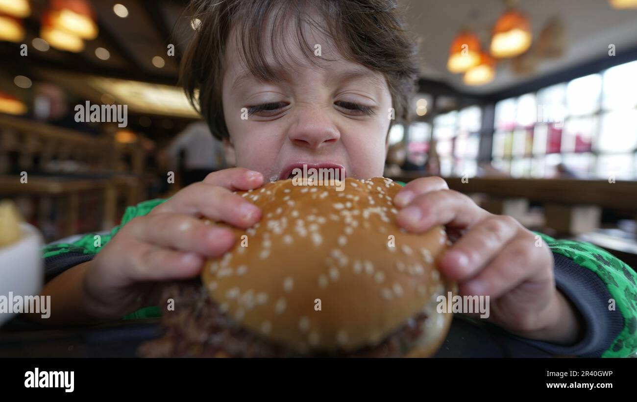 Hungry small boy eating burger sitting inside restaurant place. One ...