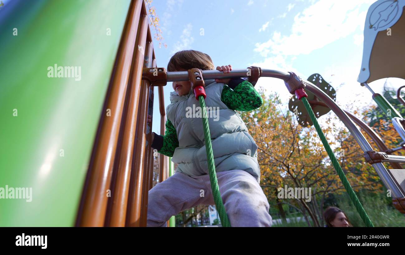 Little boy exercising outside holding in metal bar at playground ...