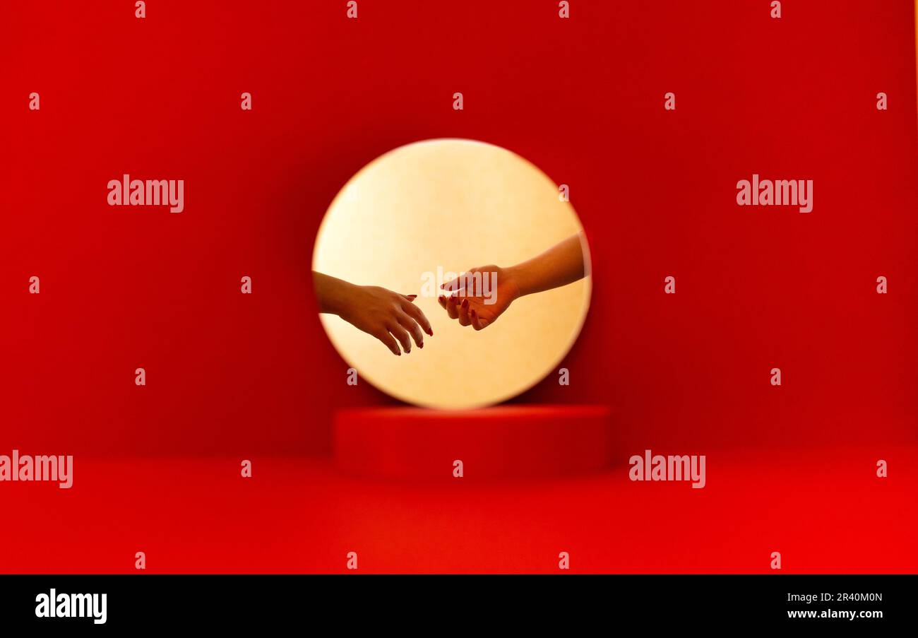 Two female reaching hands with red manicure in the reflection of round ...