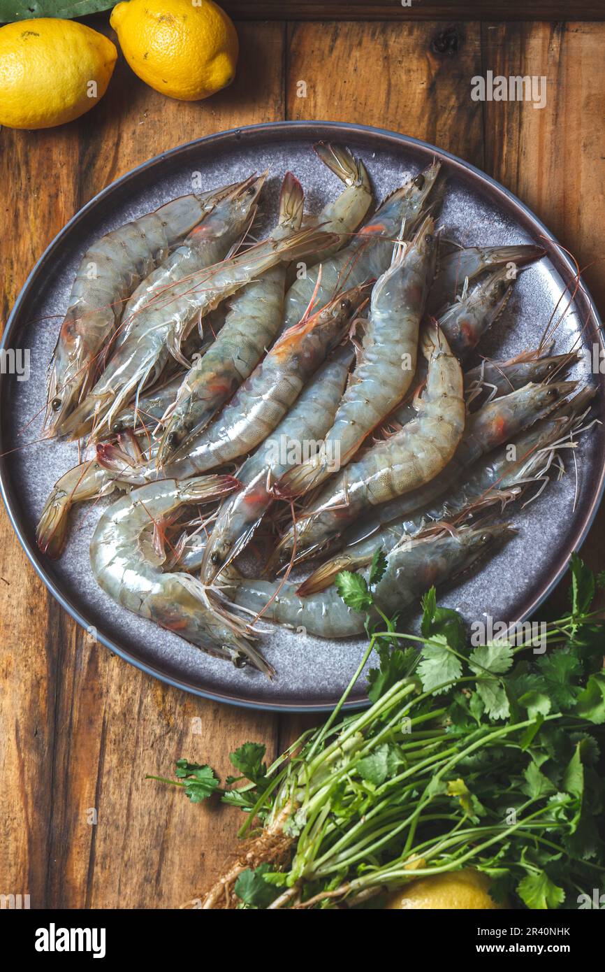 Raw shrimps prawns on gray plate with lemons and cilantro. Top view ...