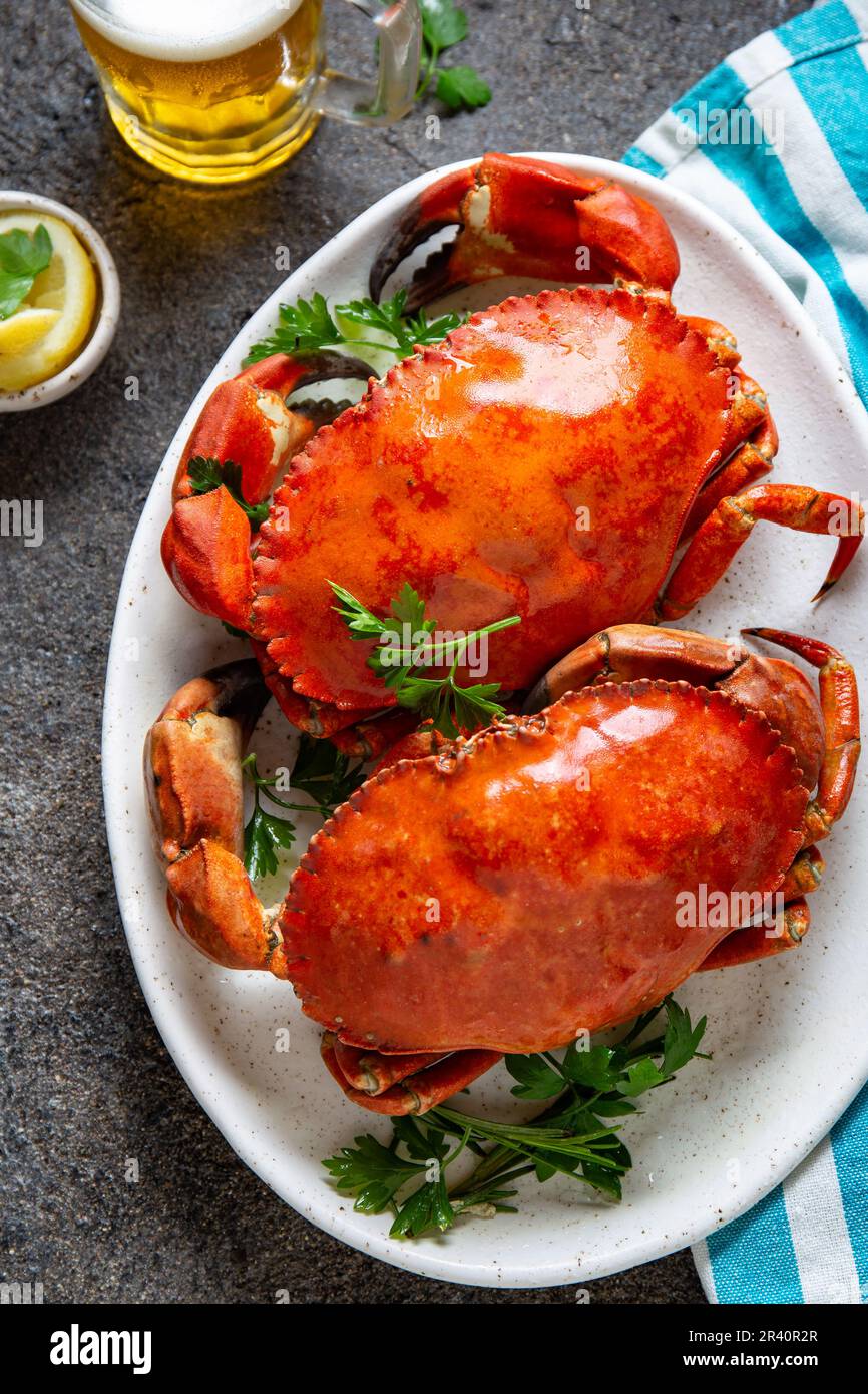 Whole cooked crabs on white plate with lemon and beer. Gray concrete ...